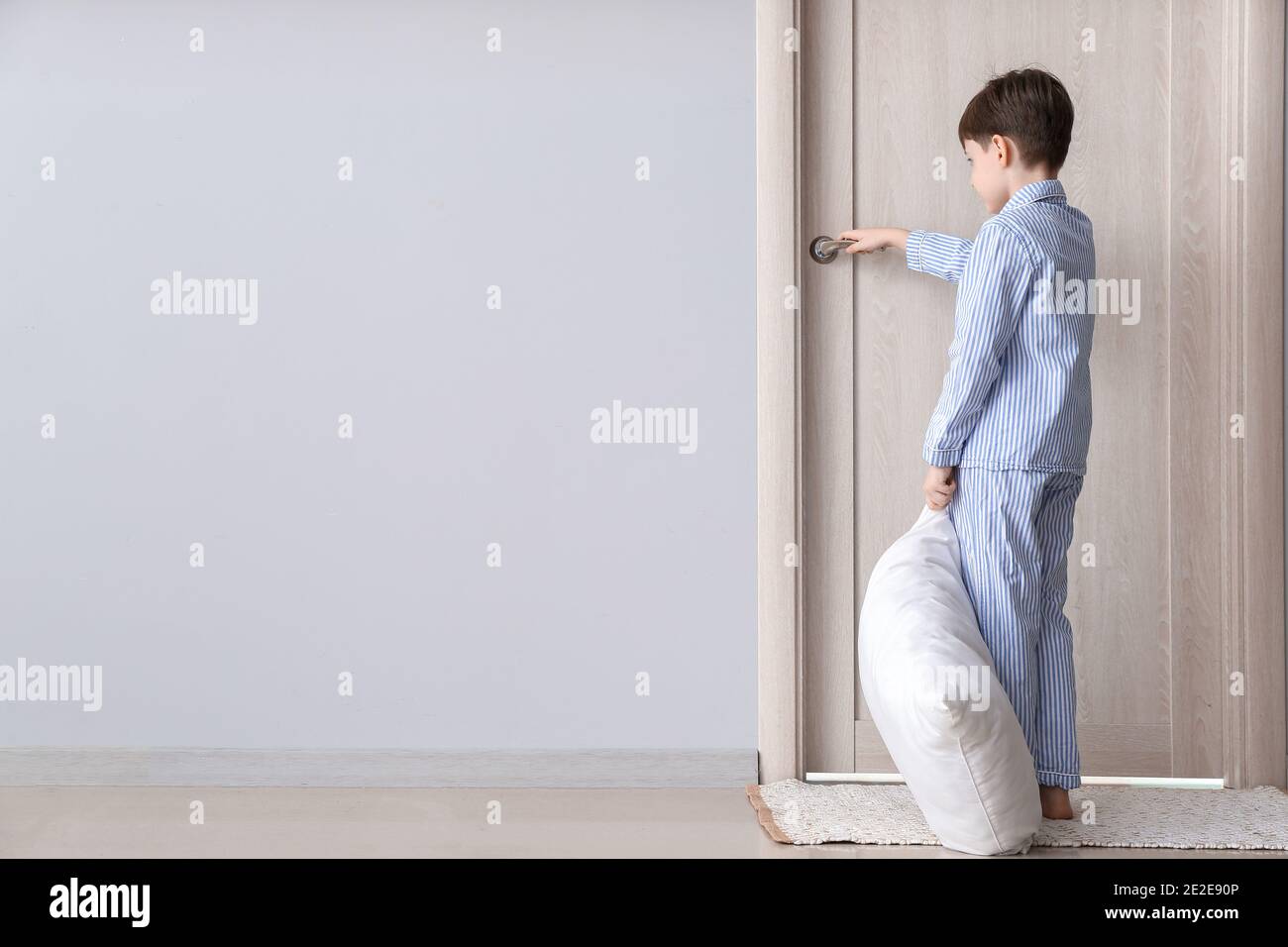 Sleepy little boy standing near closed door Stock Photo - Alamy