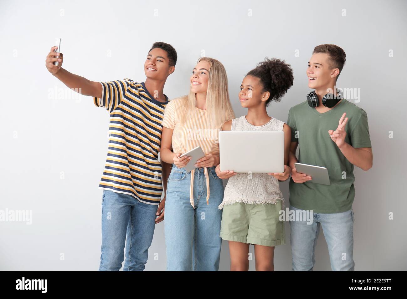 Teenagers with different devices taking selfie on light background ...