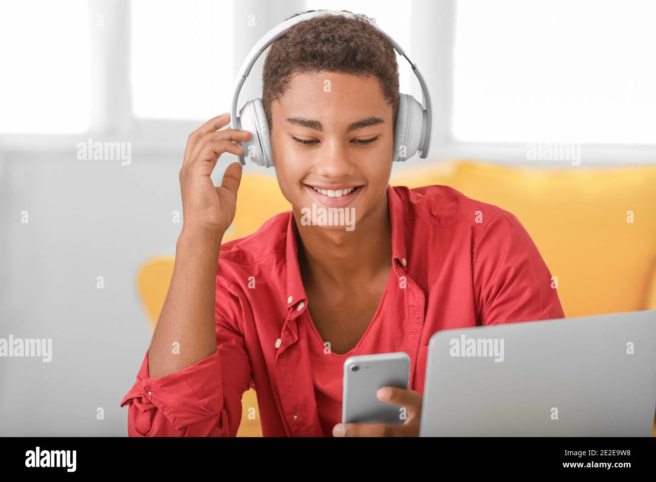 Teenage African-American boy with headphones and mobile phone at home ...