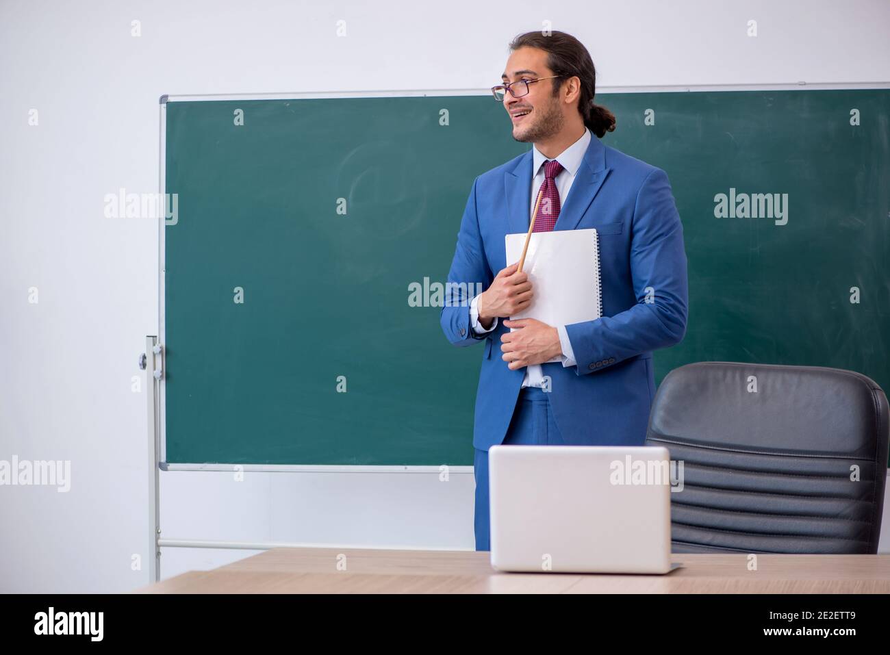 Young teacher in suit in front of green board Stock Photo - Alamy