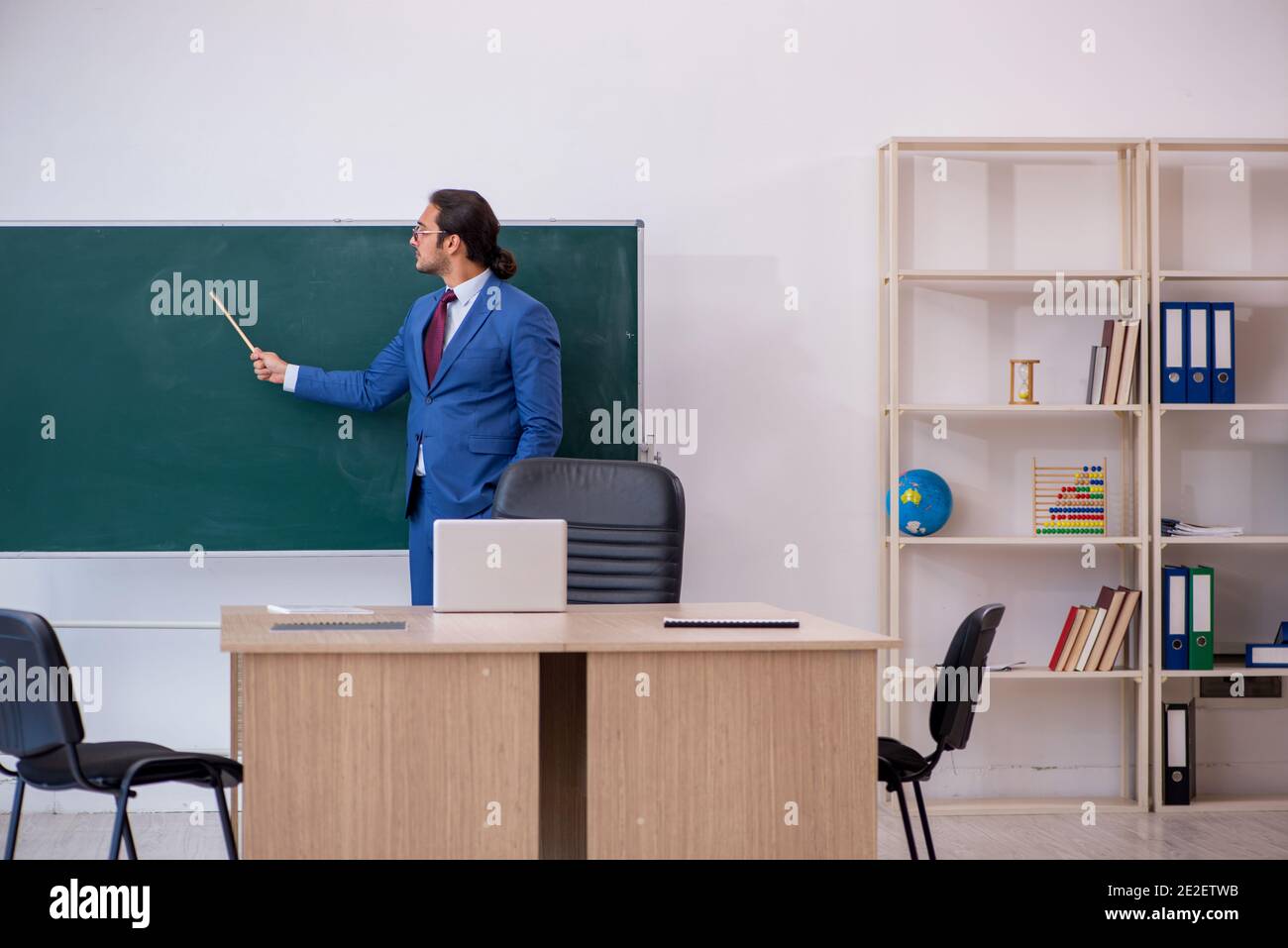 Young teacher in suit in front of green board Stock Photo - Alamy