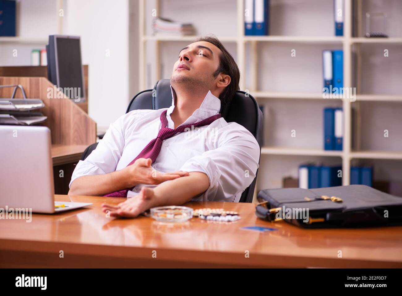 Young drug addicted male employee sitting at workplace Stock Photo - Alamy