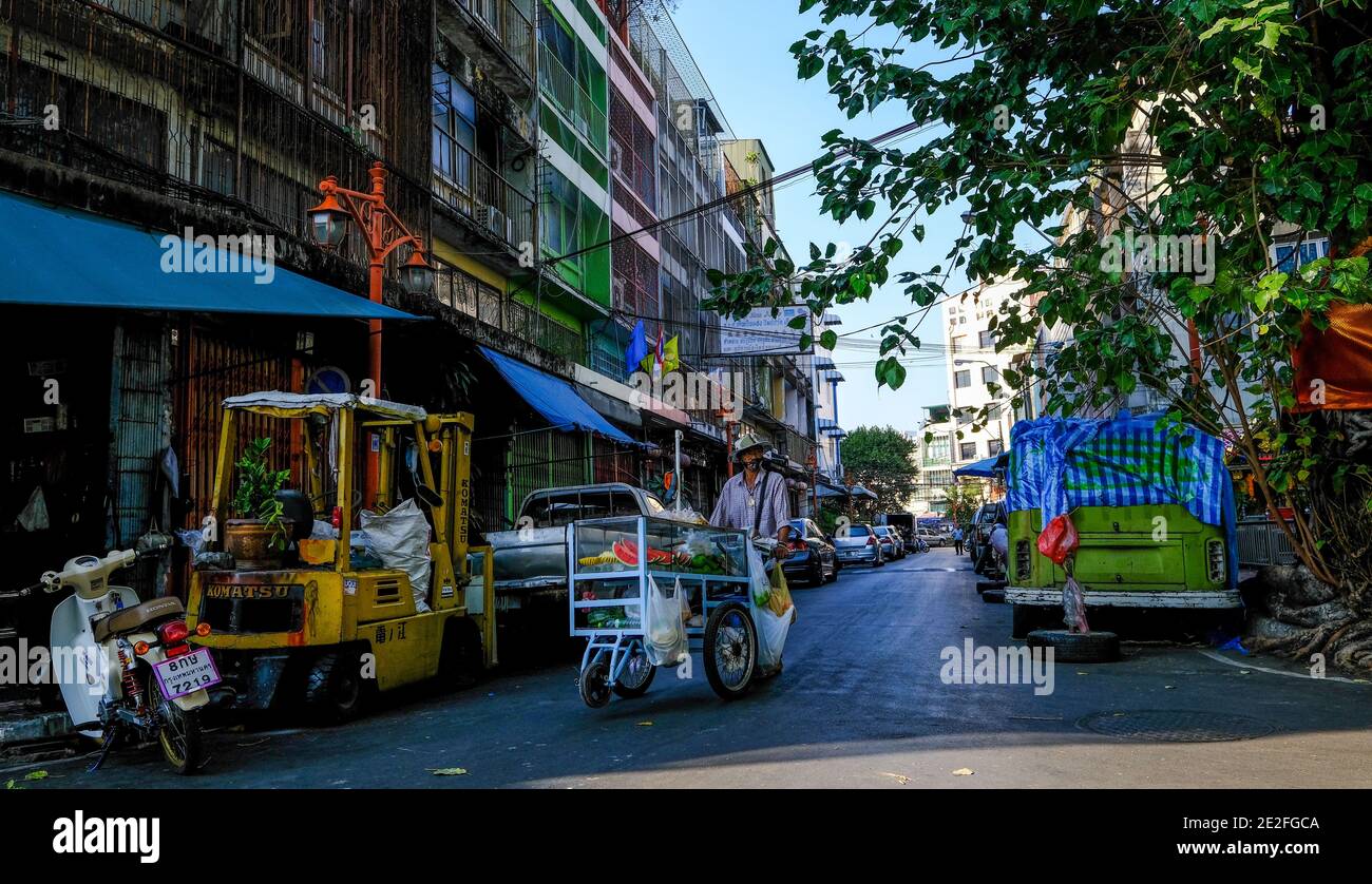 A mobile fruit vendor pushes his cart around the Talat Noi area of ...