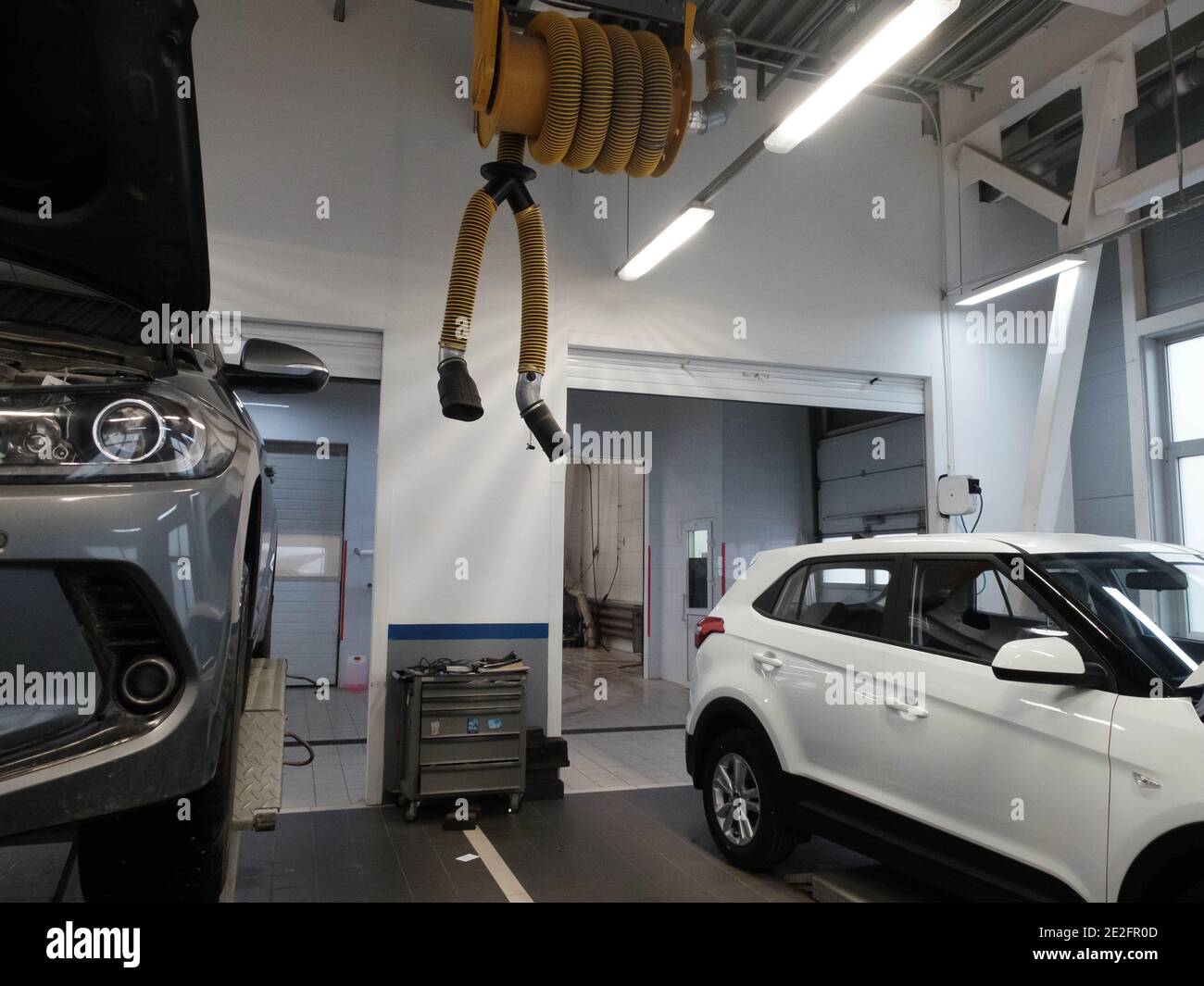 Car with the open engine hood on the lift and white SUV in the car ...