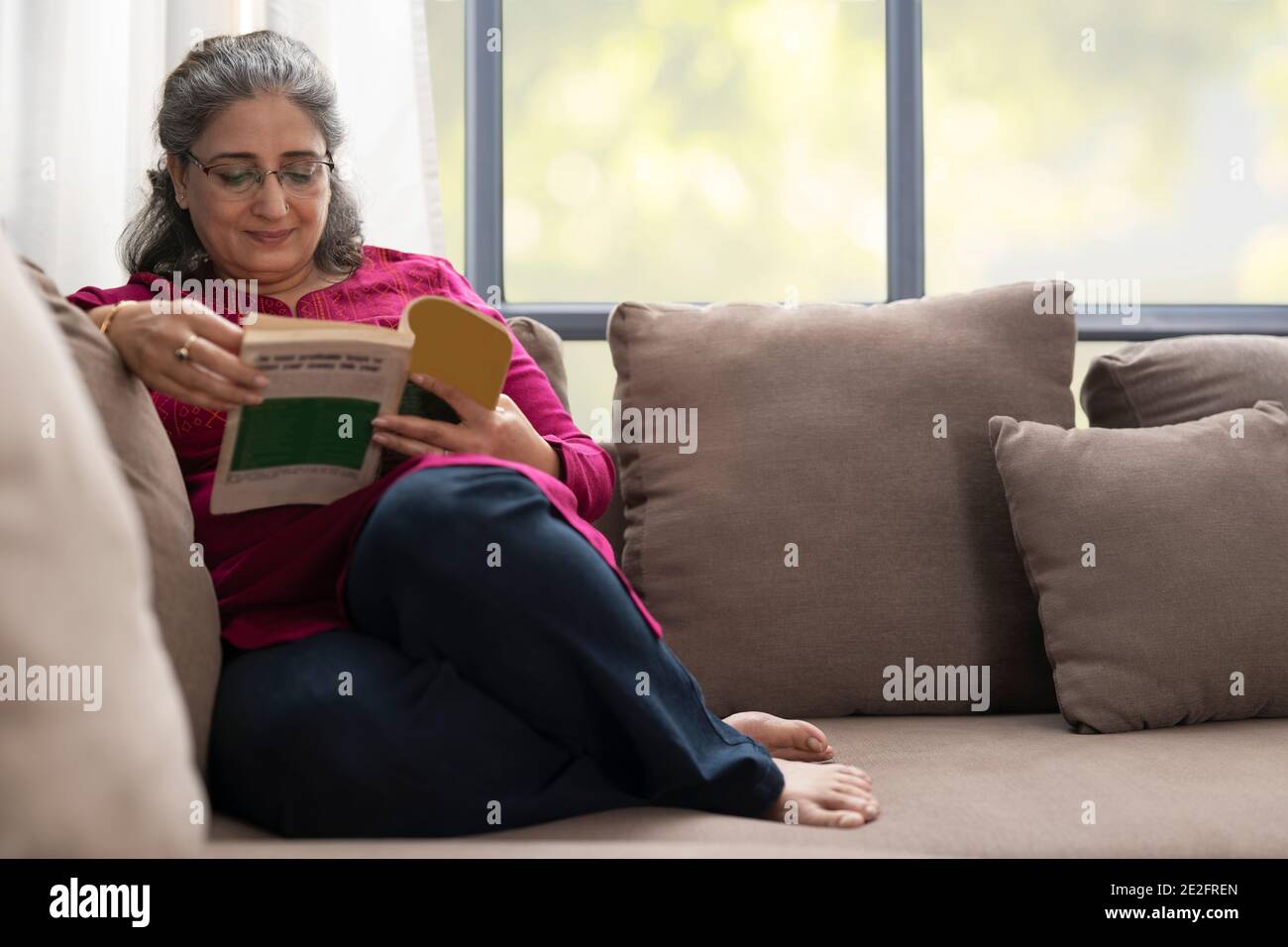 AN OLD WOMAN READING A BOOK WHILE SITTING COMFORTABLY ON SOFA Stock ...