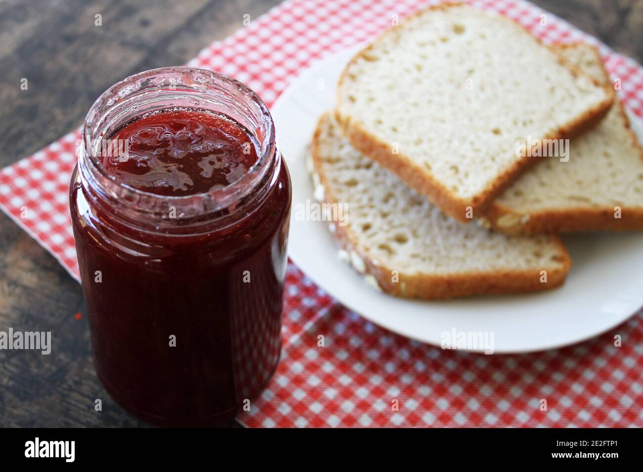A jar of strawberry jam next to three slices of bread against a rustic ...