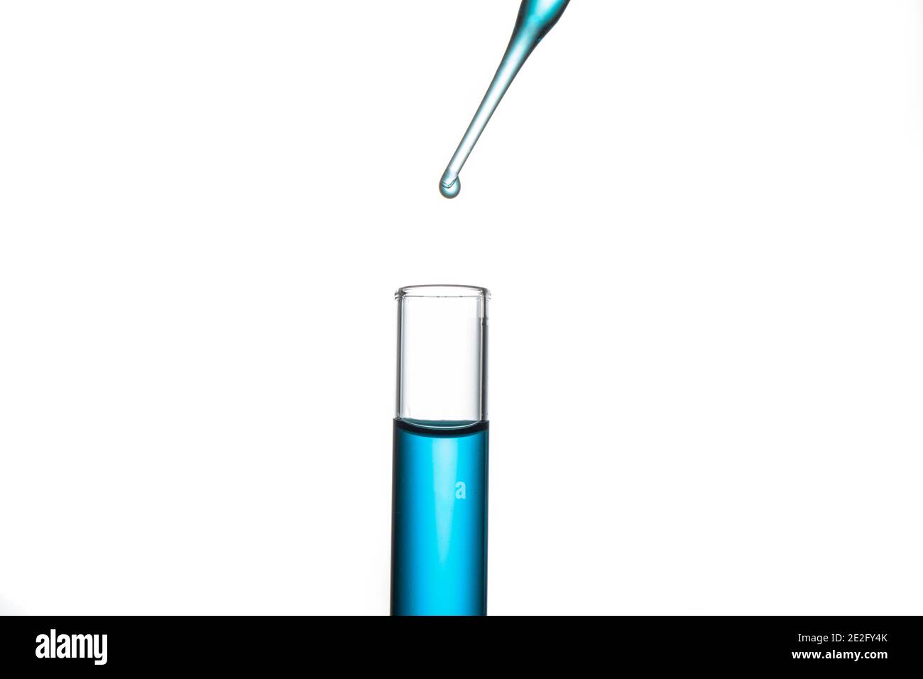 Pipette tip dropping bright blue liquid into a test tube isolated on a ...