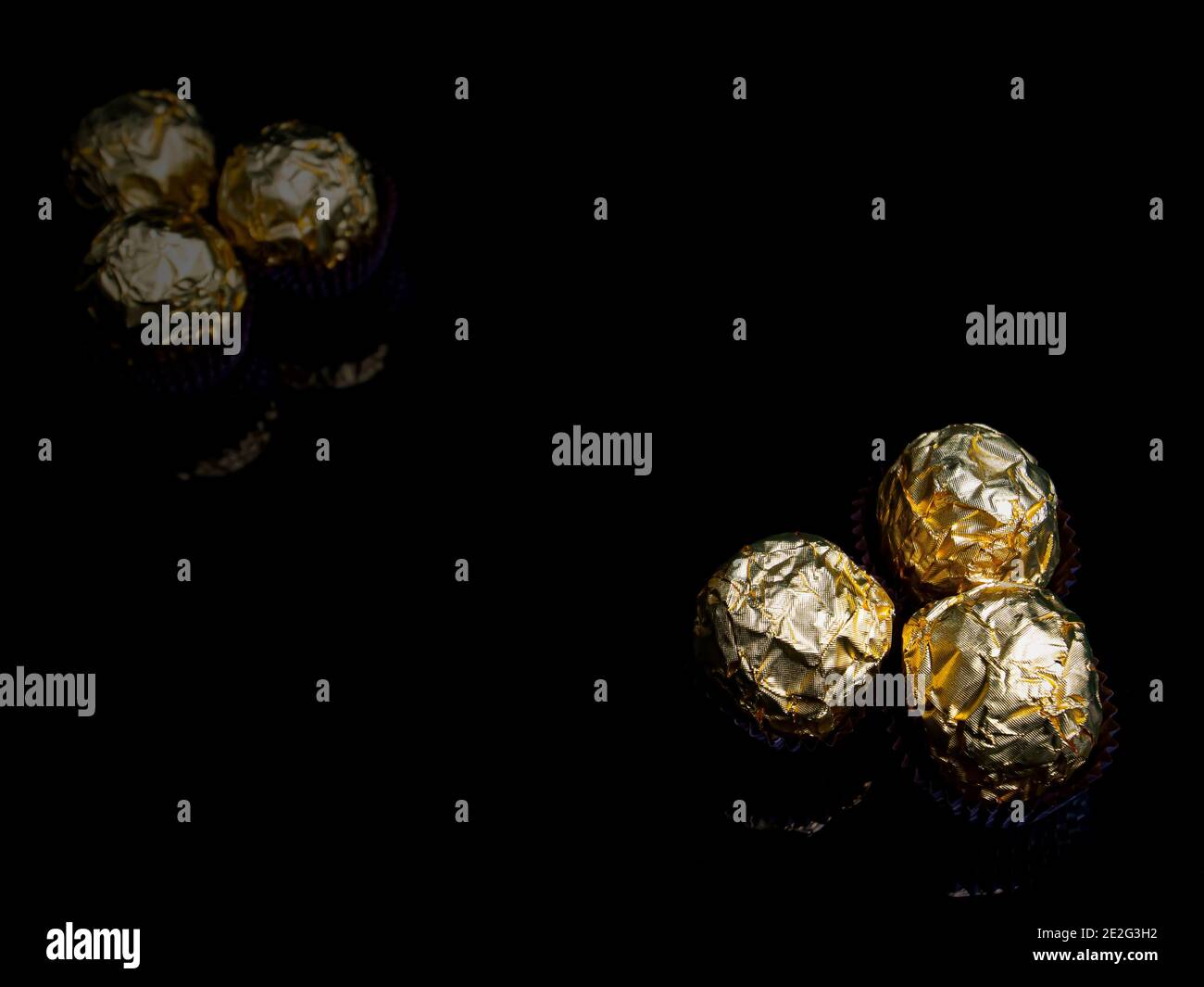 Round candies in golden foil on a black background. Wrapped chocolates ...