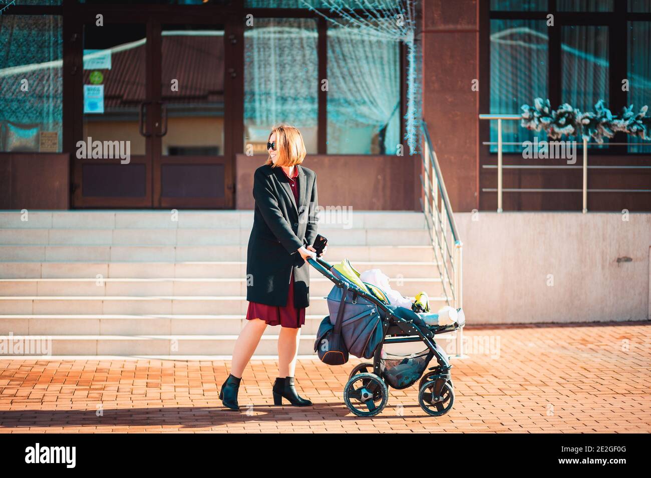 A young fashionable mother is pushing a stroller down the street ...