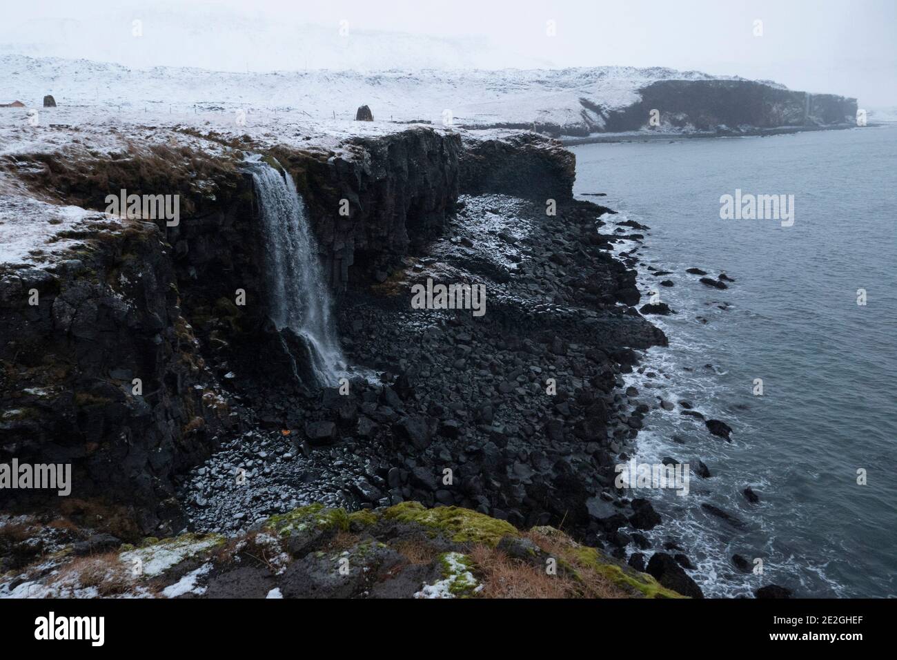 Majestic snowy waterfall over ocean cliff, Arnastapi, Iceland Stock ...
