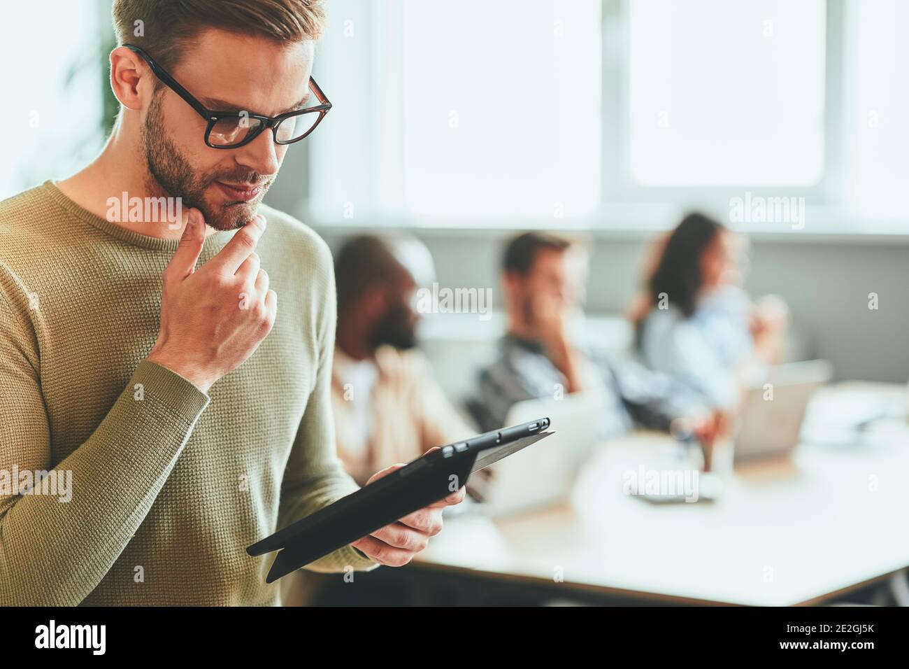 Puzzled young office worker using tablet at workplace Stock Photo - Alamy