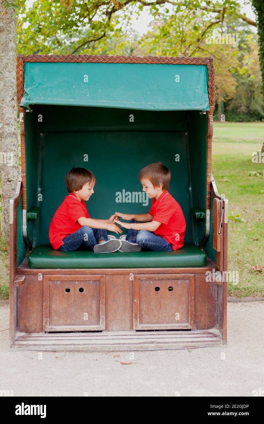 Two kids, brothers,sitting in a sheltered bench, playing hand clapping ...