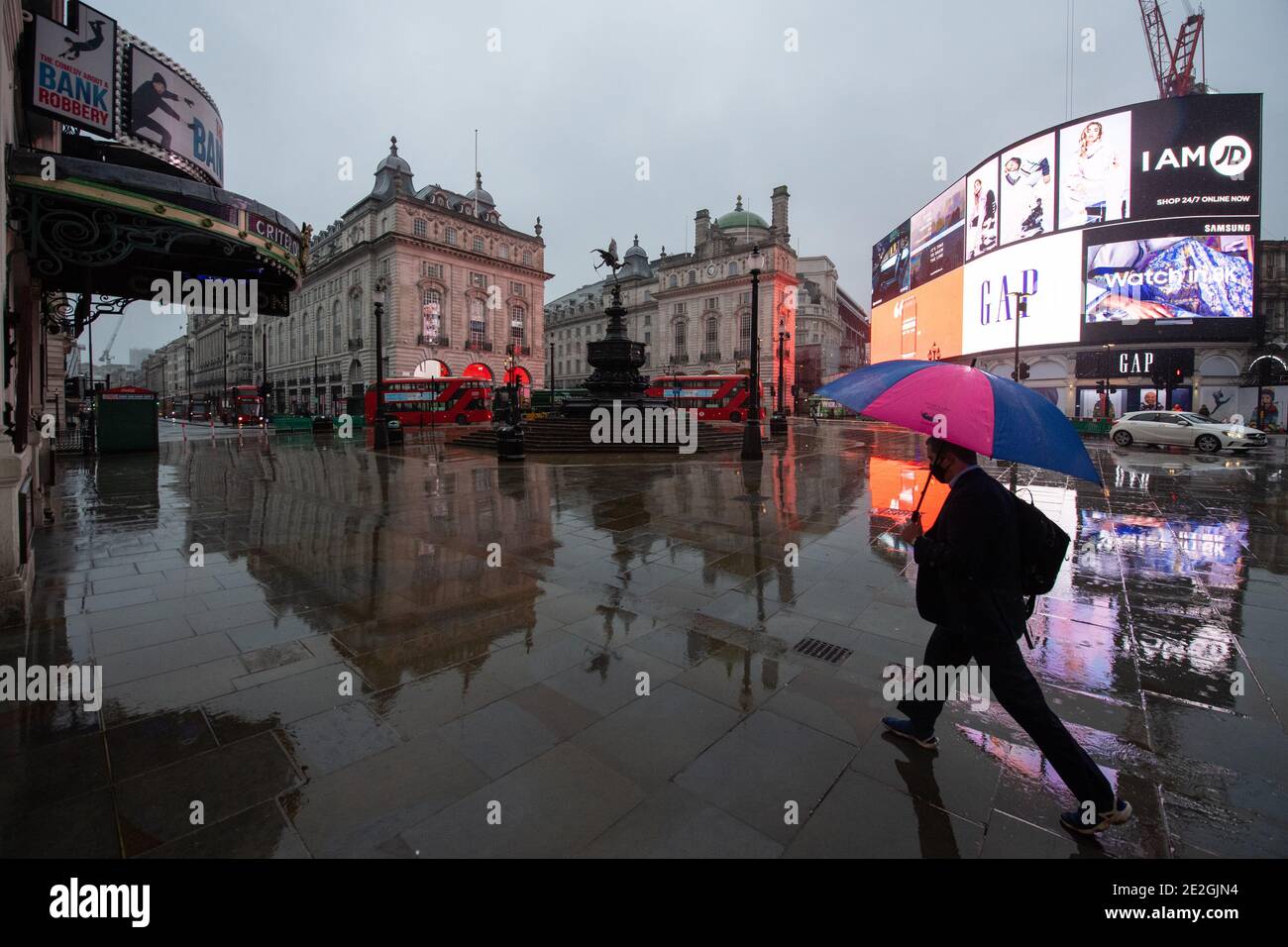 A man with an umbrella walks through a near empty Piccadilly Circus in ...