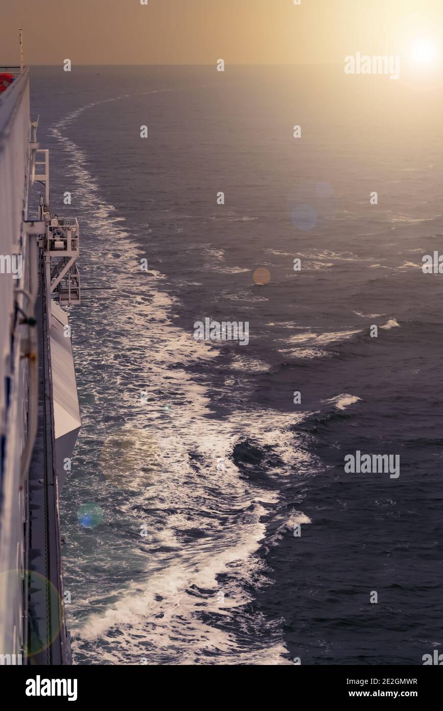 Cruise ship sailing at sea with wake waves and hand rails in the sunset ...