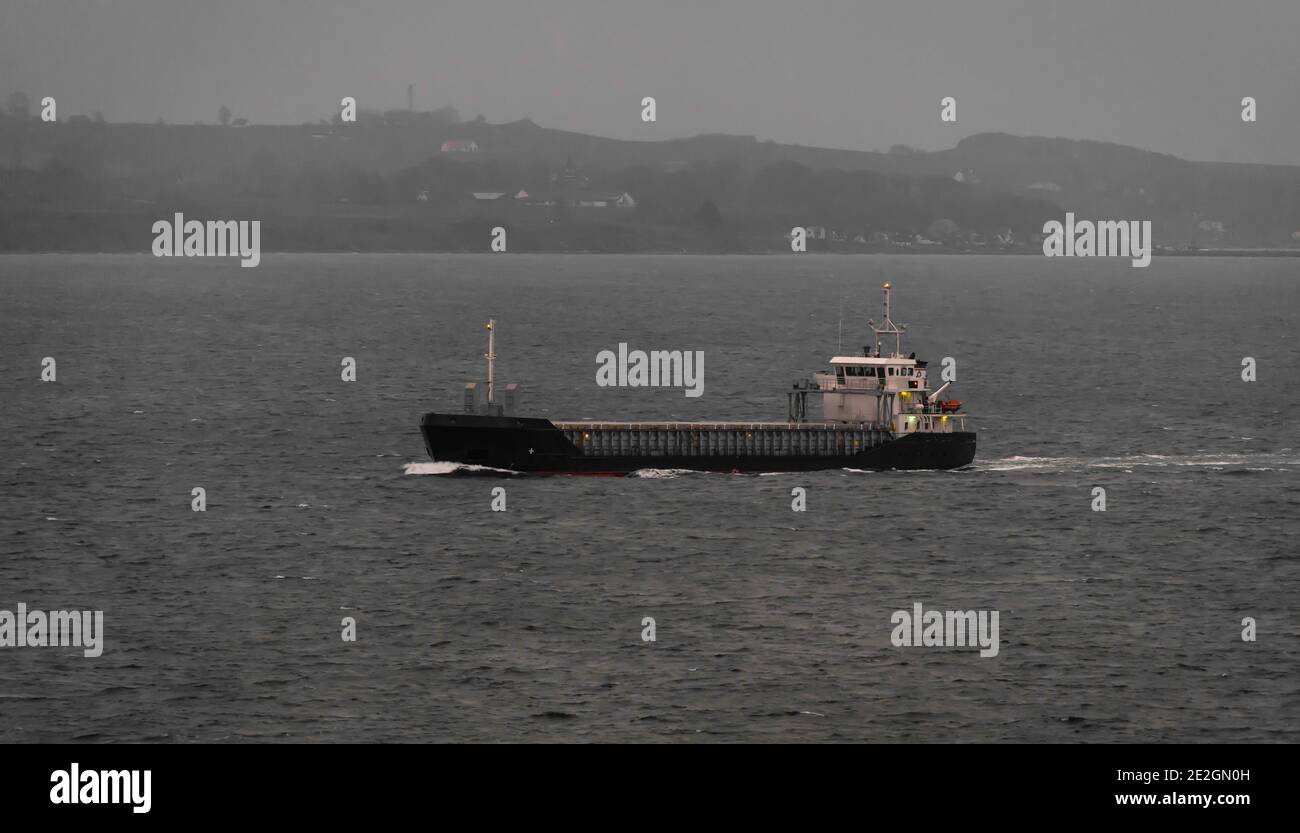 Cargo vessel sailing at sea along a coastline on a dull grey day Stock ...