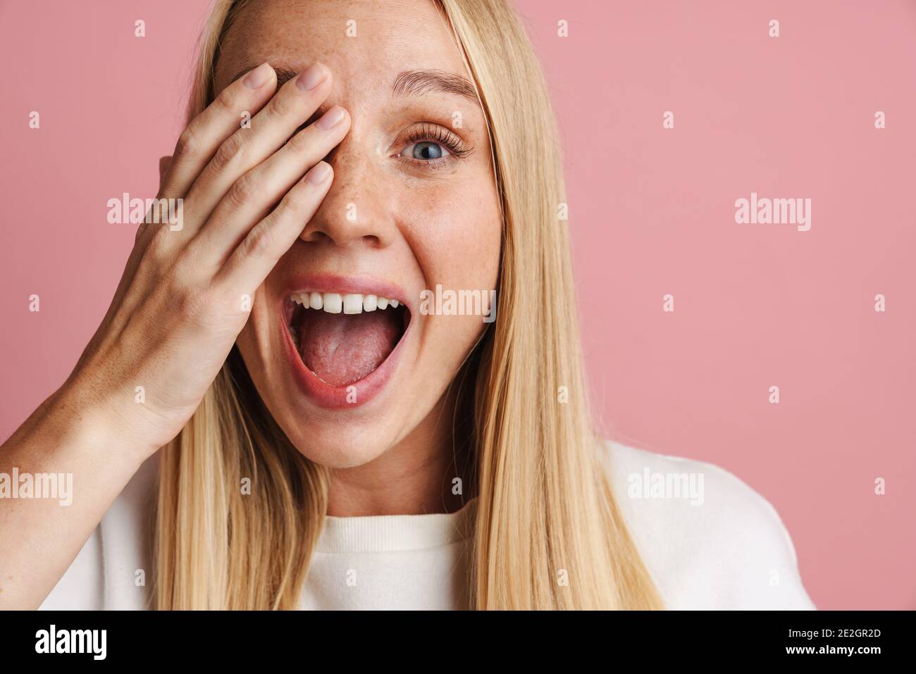 Excited beautiful girl screaming and covering her eye isolated over ...