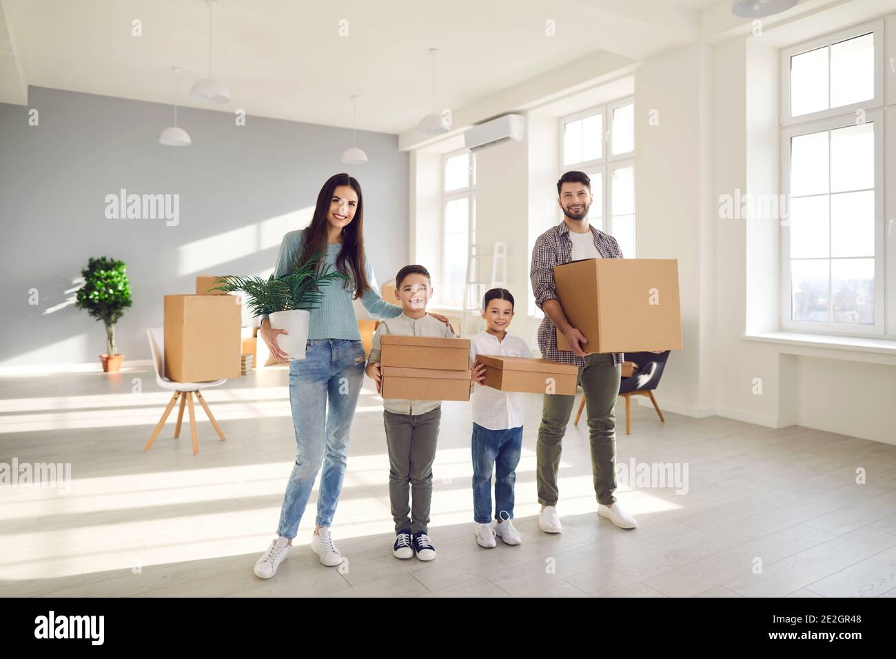 Happy smiling family with kids carrying cardboard boxes while moving ...