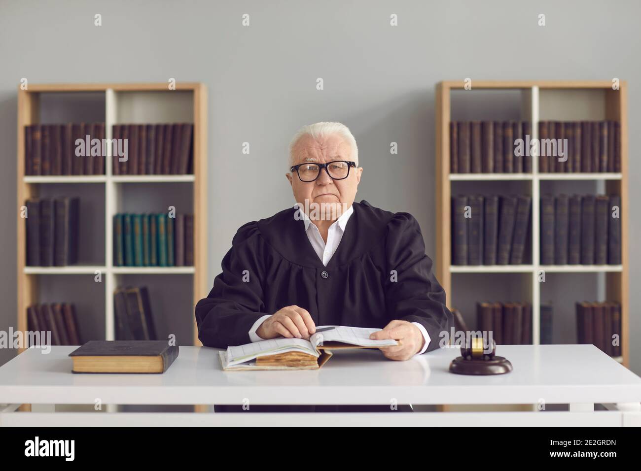 Portrait of serious senior judge sitting at table with open book in ...