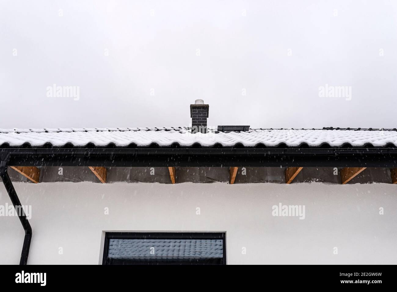 The roof of a detached house is covered with snow against a cloudy sky ...