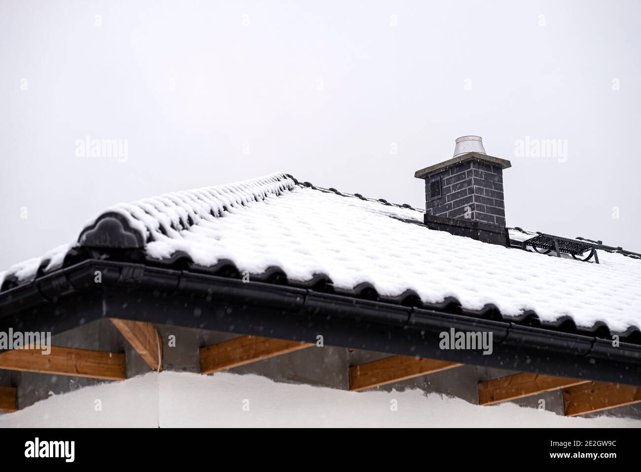 The roof of a detached house is covered with snow against a cloudy sky ...
