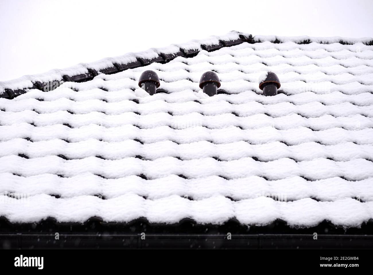 The roof of a single-family house is covered with snow against a cloudy ...