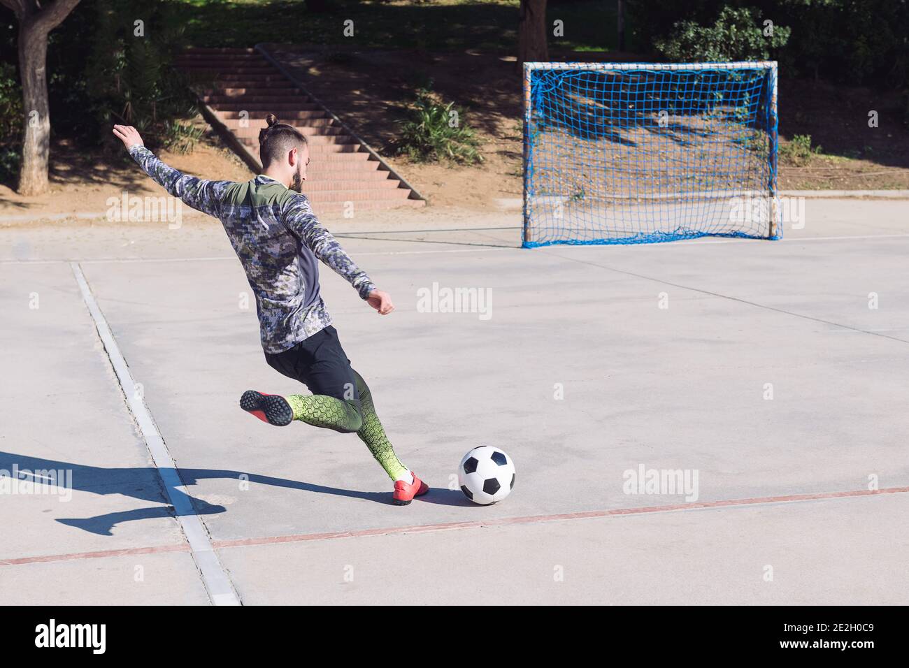 rear view of a football player kicking the soccer ball into an empty ...