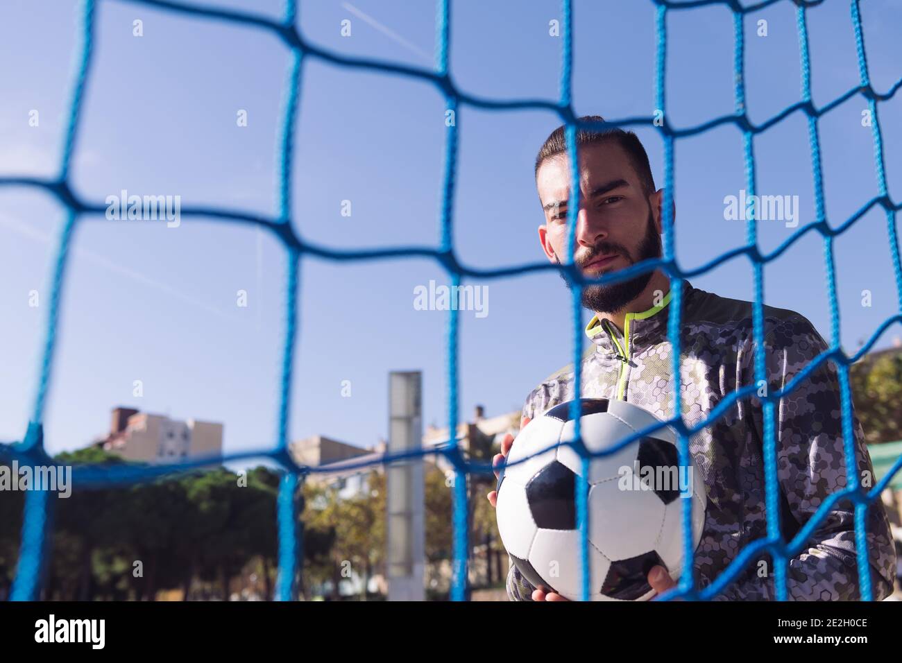 handsome soccer player looking at camera through the goal net with the ...