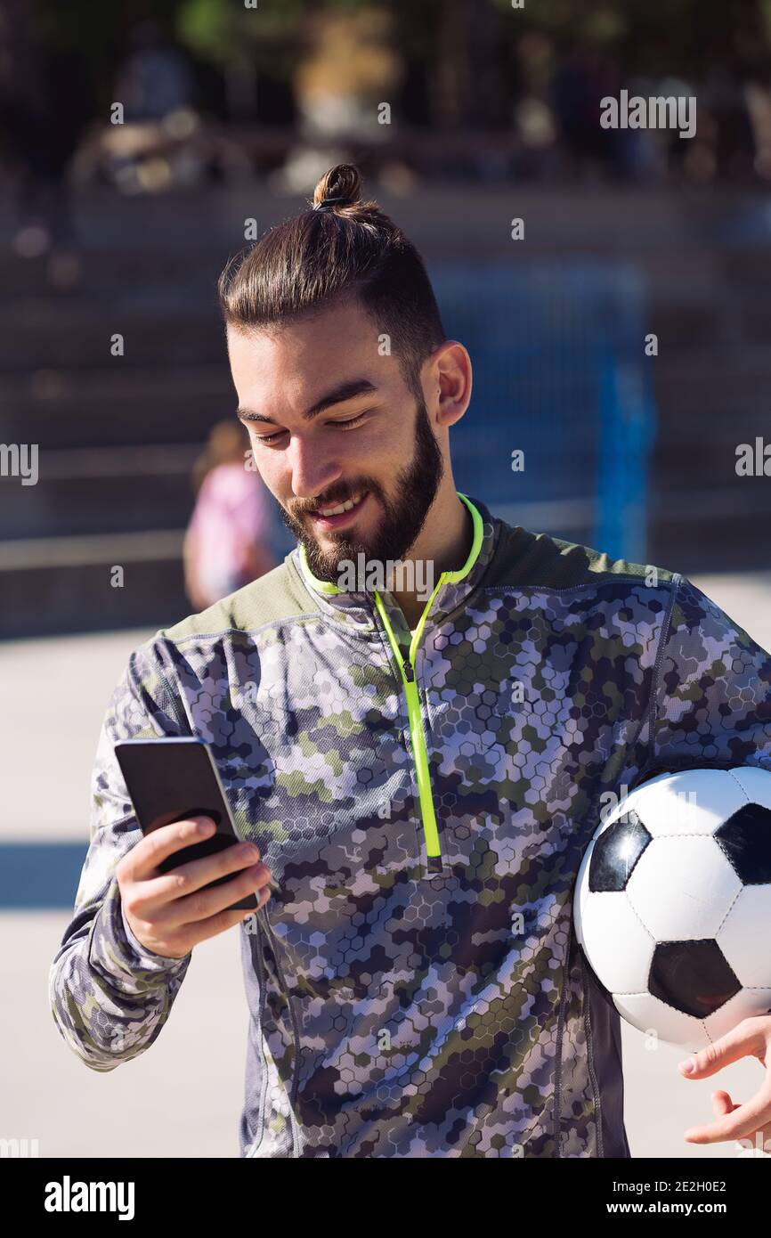 fashionable sportsman with a soccer ball smiles consulting his mobile ...