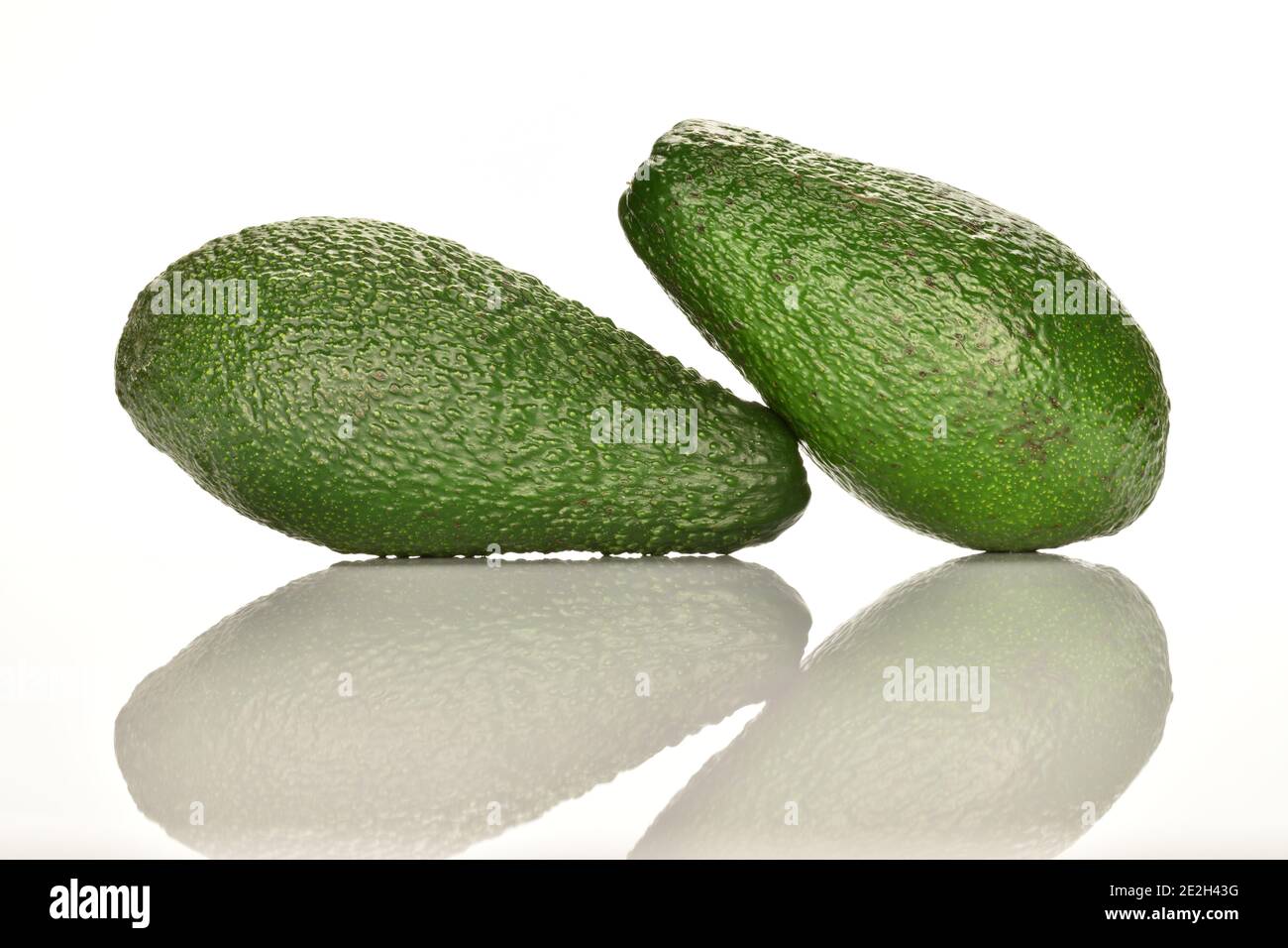 Two whole oval dark green ripe organic diet avocados, lying one on top ...