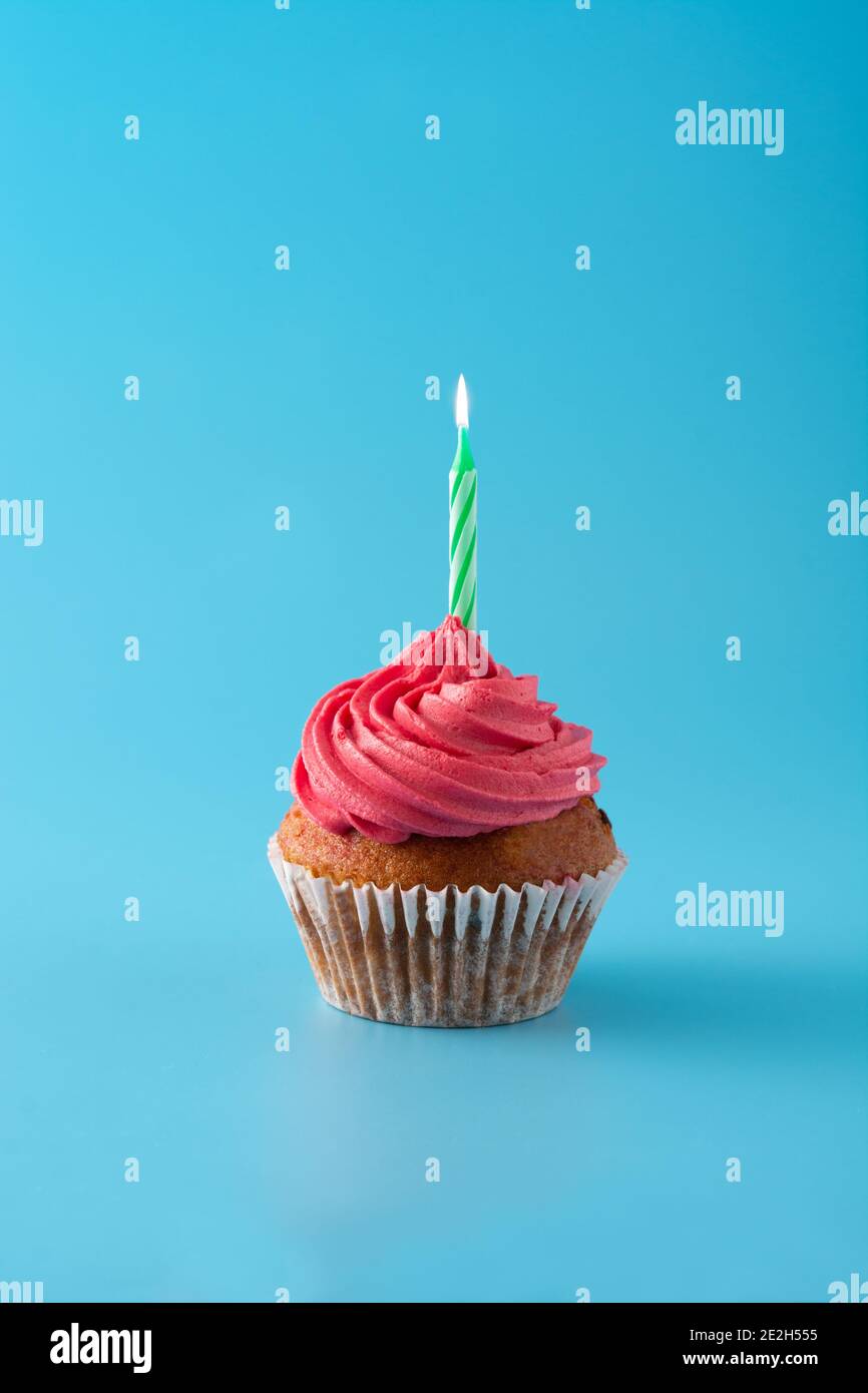 Pink birthday cupcake with green candle on blue background Stock Photo ...