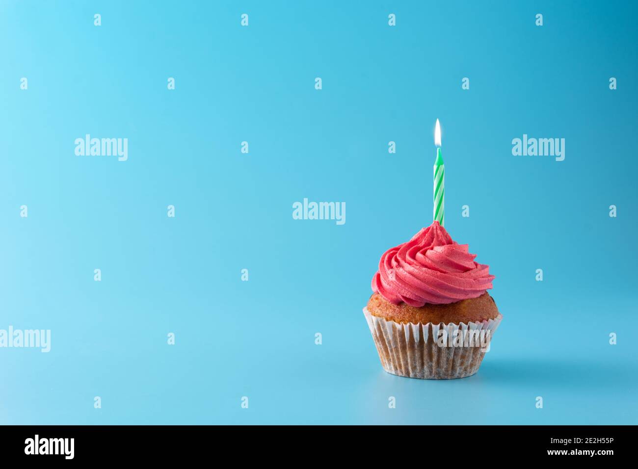 Pink birthday cupcake with green candle on blue background Stock Photo ...
