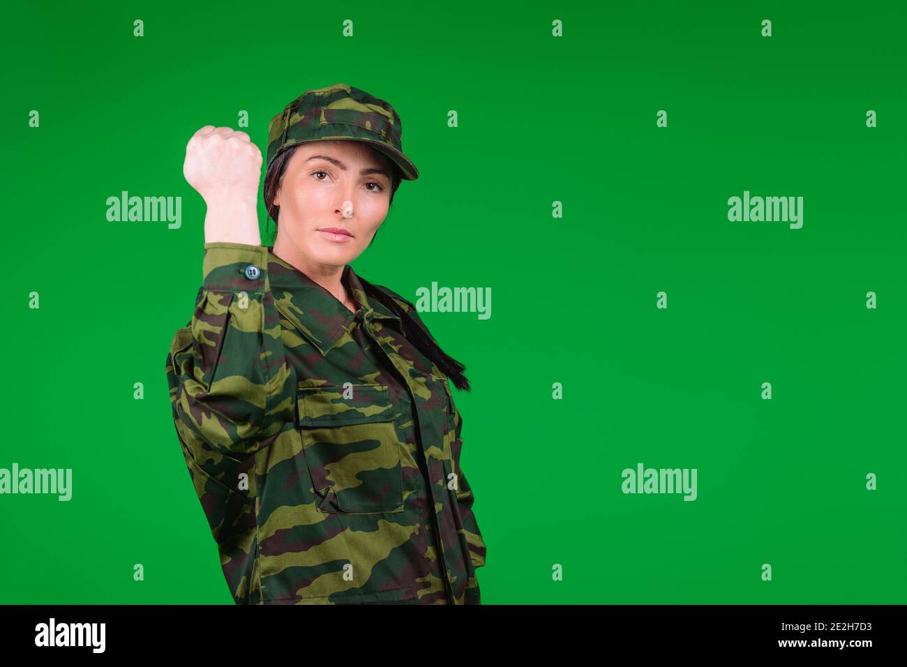 Young woman in military uniform shows her fist to the camera on a green ...