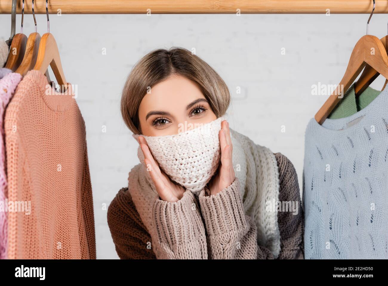 Woman covering face with scarf near sweaters on hanger rack on white ...