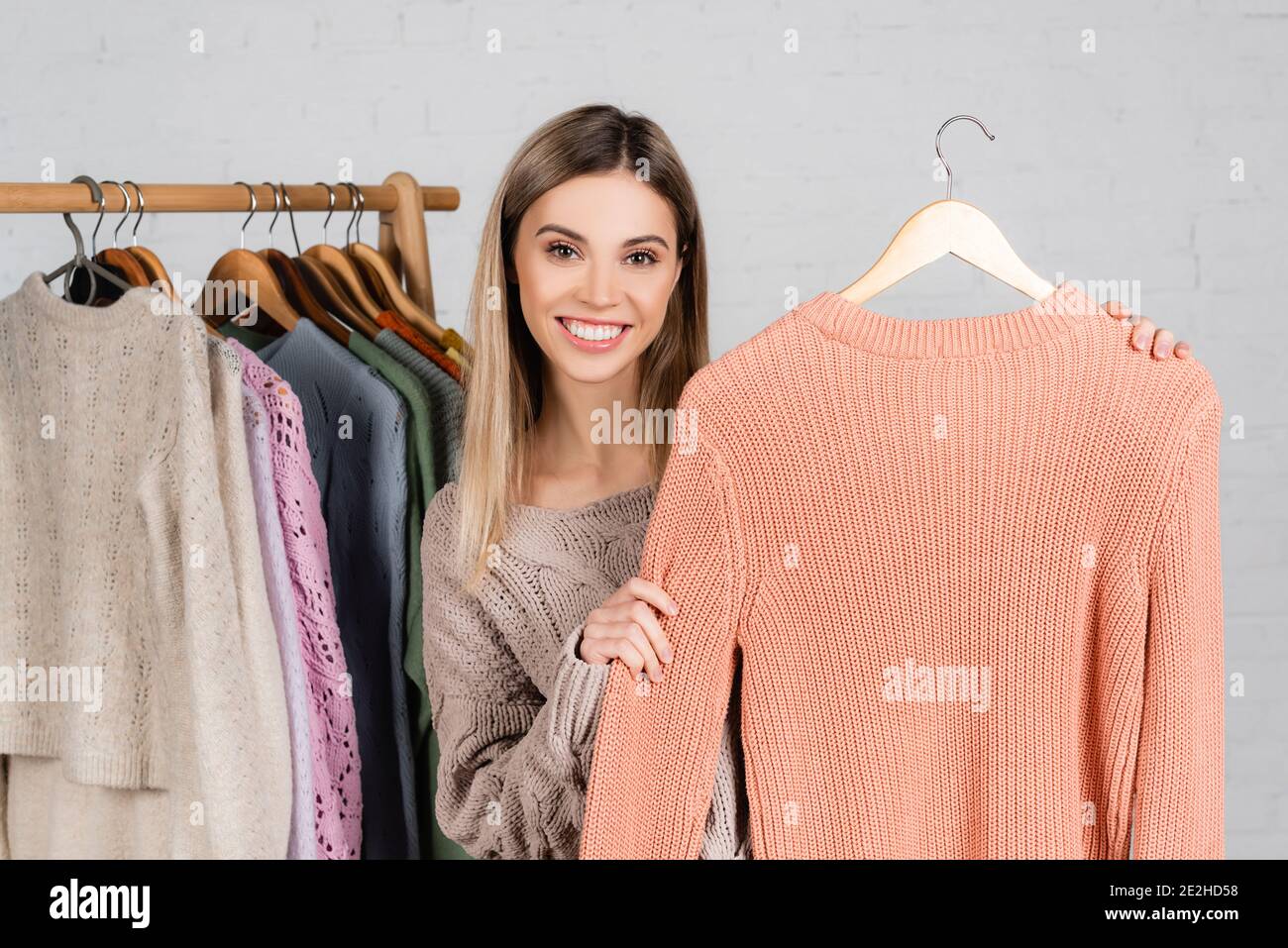 Positive woman holding cozy sweater near knitwear on hanger rack on ...