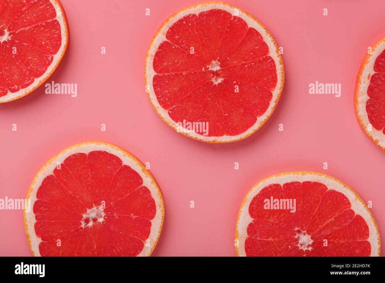 Patterns of slices of juicy grapefruit on a pink background, a ...