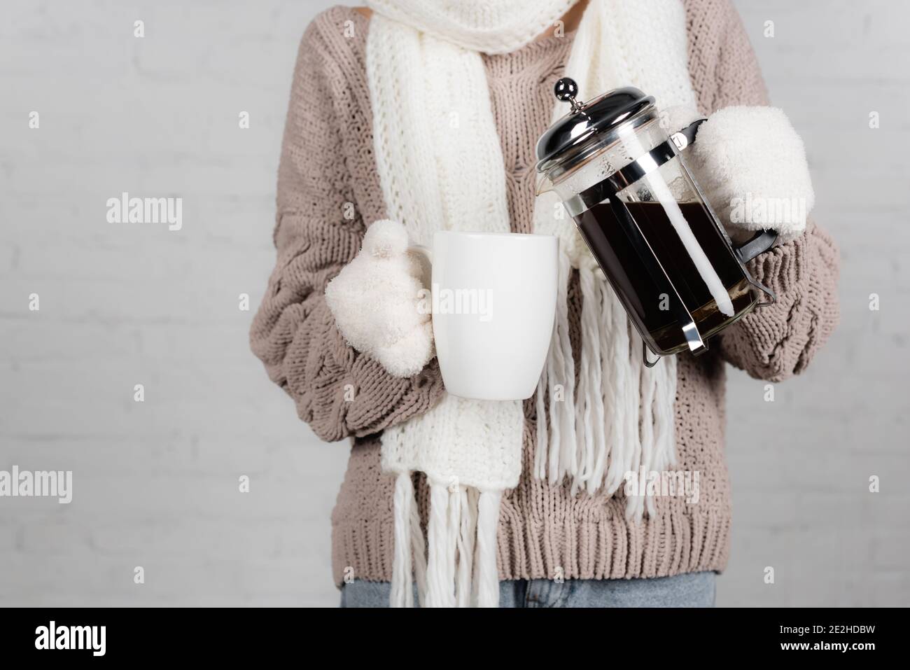 Cropped view of woman in knitted sweater, scarf and warm gloves pouring ...