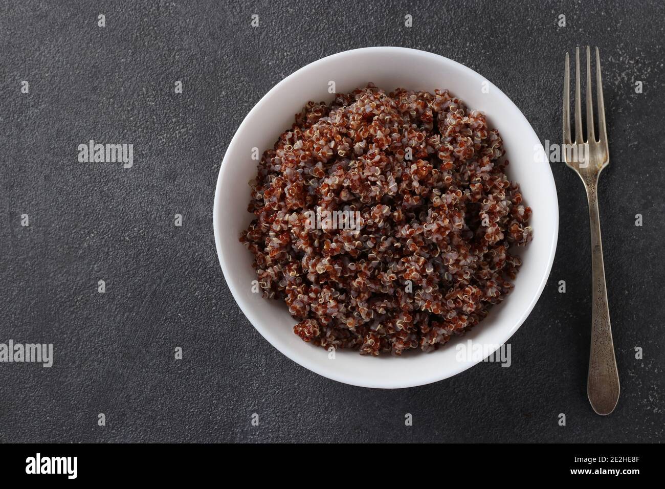 Cooked red quinoa in a white plate on a dark gray background. View from above. Space for text ...