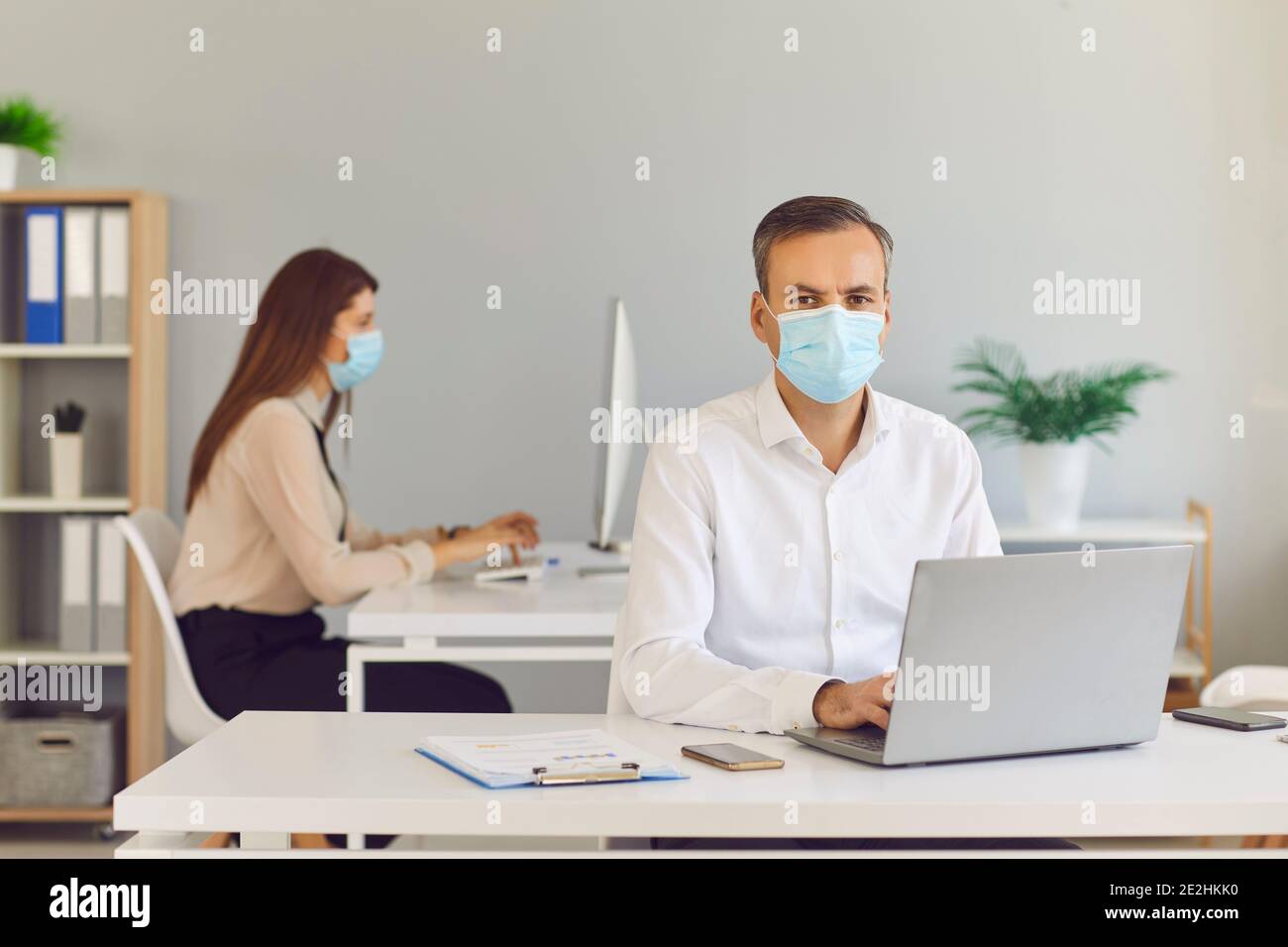 Serious young man in medical face mask working in the company office ...