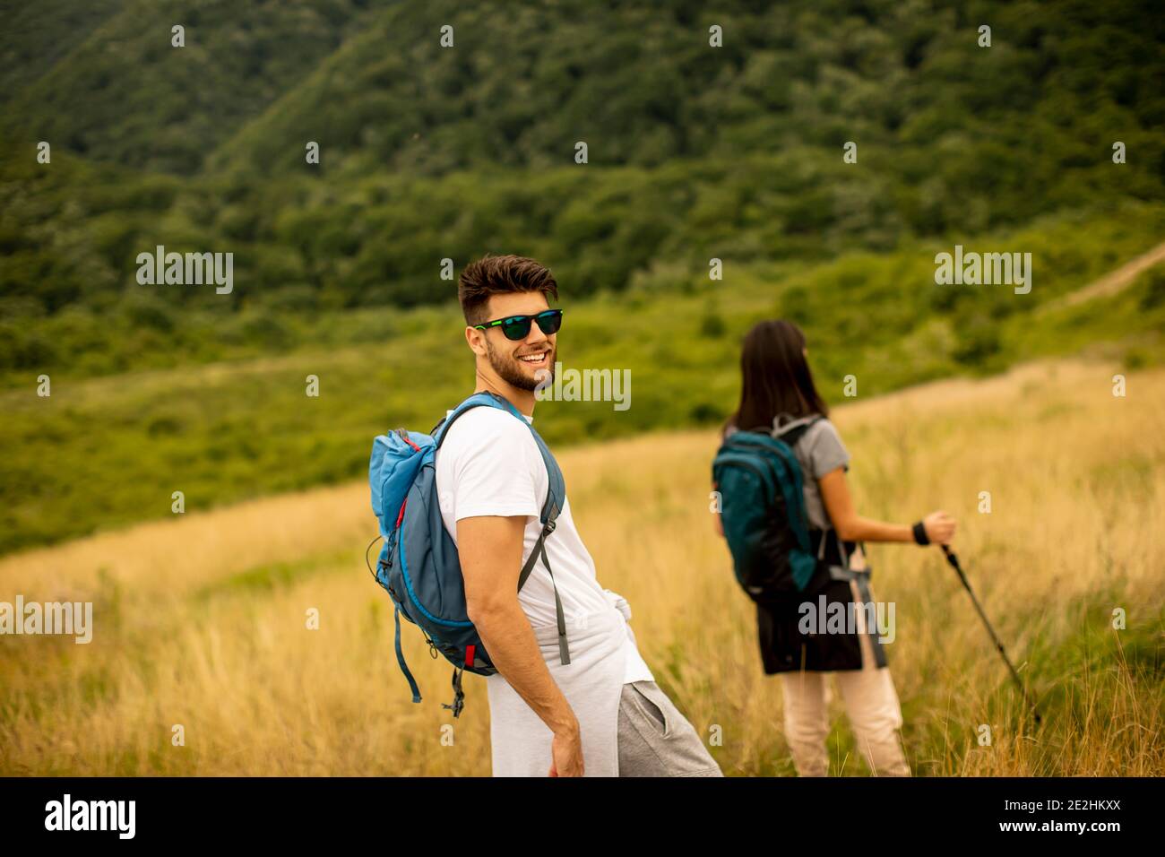 Smiling young couple walking with backpacks over green hills Stock ...