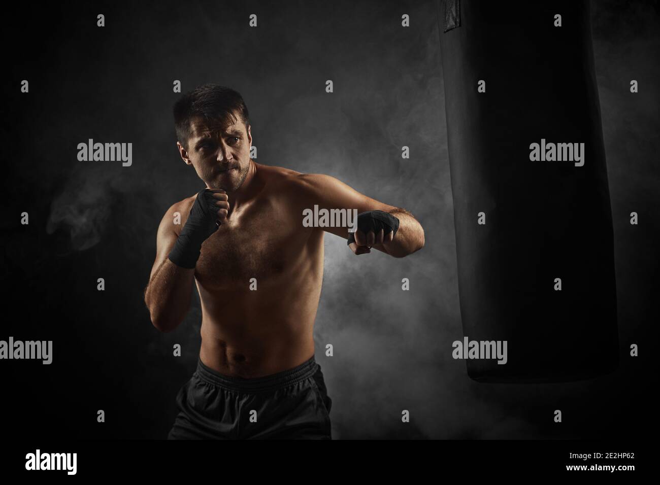 sporty shirtless boxer in black boxing wraps punching in boxing bag on ...