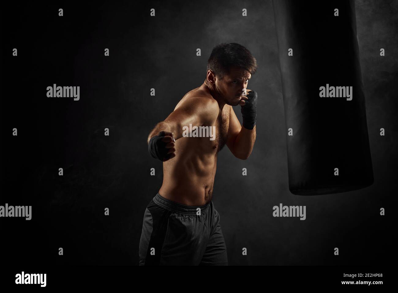 Male boxer training defense and attacks in boxing bag on black ...