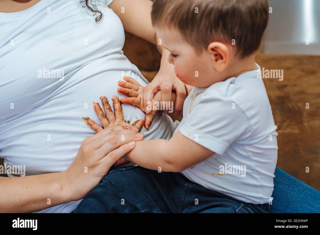 Child making chocolate handprint on pregnant mother's belly while ...