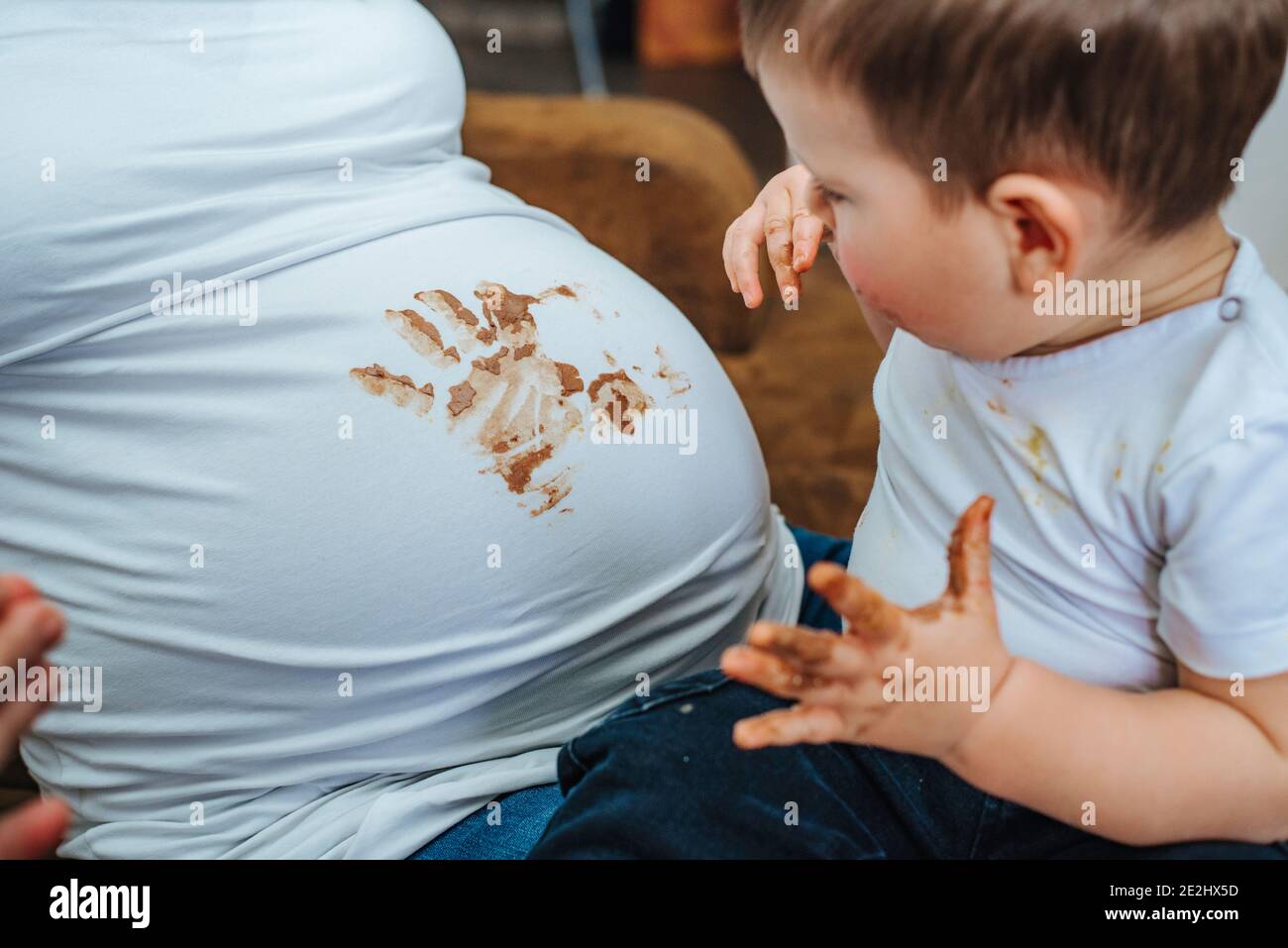 Child making chocolate handprint on pregnant mother's belly while ...