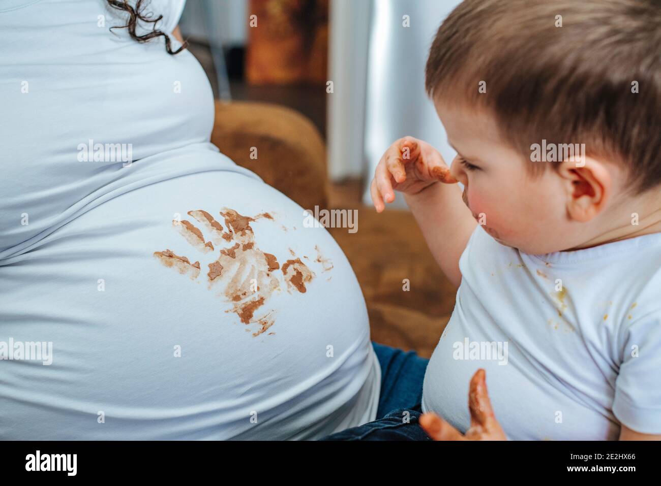 Child making chocolate handprint on pregnant mother's belly while ...
