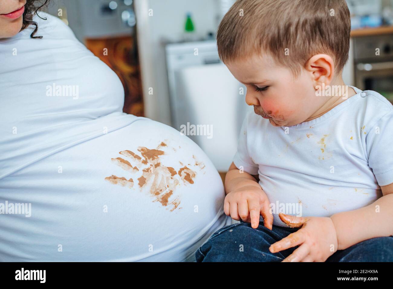Child making chocolate handprint on pregnant mother's belly while ...