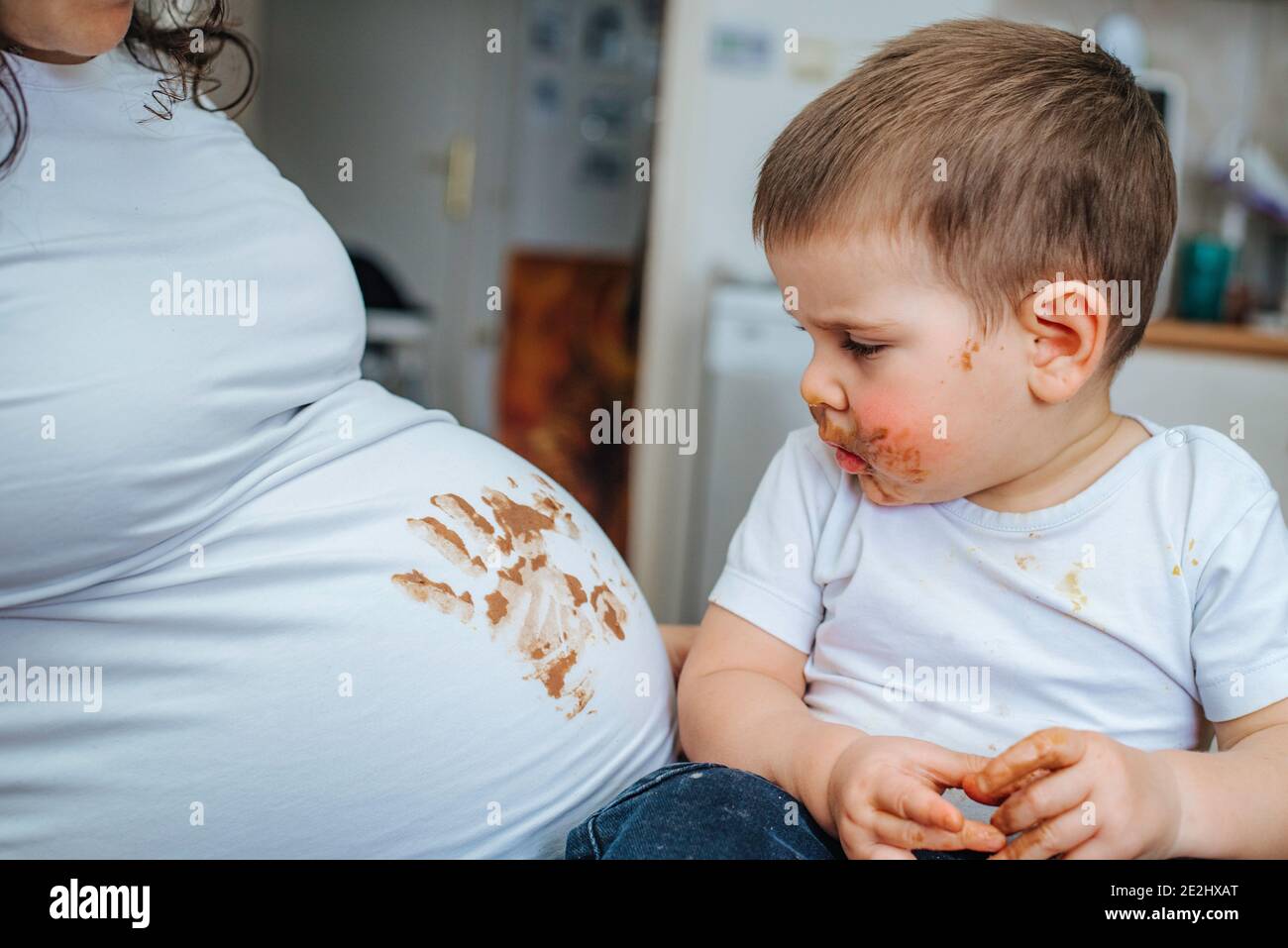 Child making chocolate handprint on pregnant mother's belly while ...