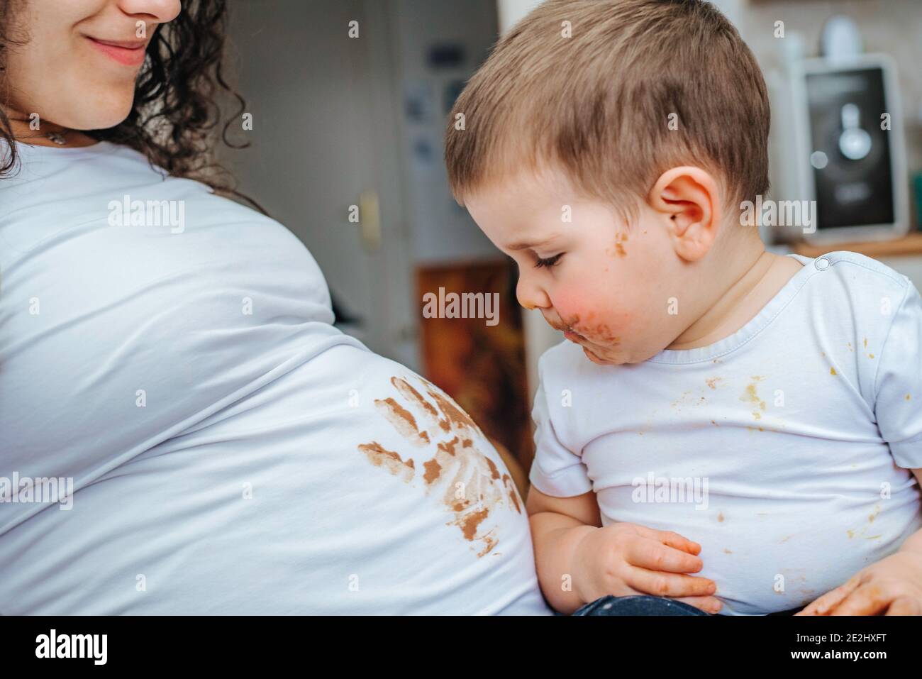 Child making chocolate handprint on pregnant mother's belly while ...