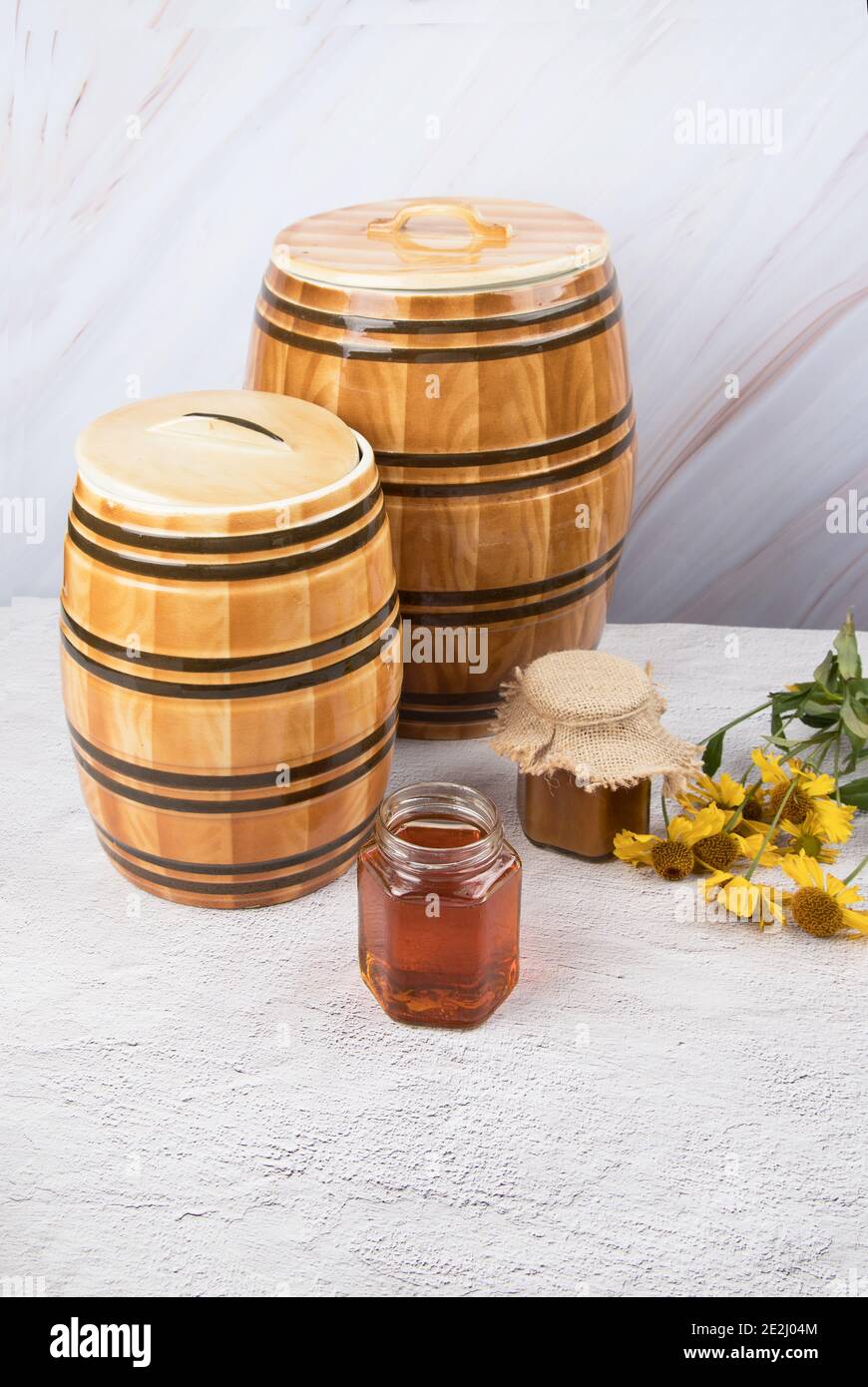 Two ceramic barrels and two glass jars with honey and yellow flowers on ...