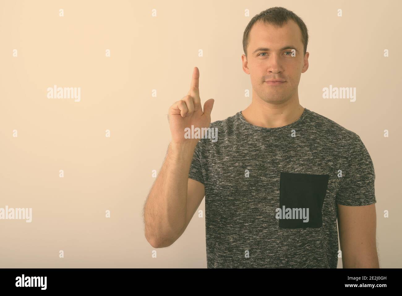 Studio shot of young muscular man pointing finger up against white ...