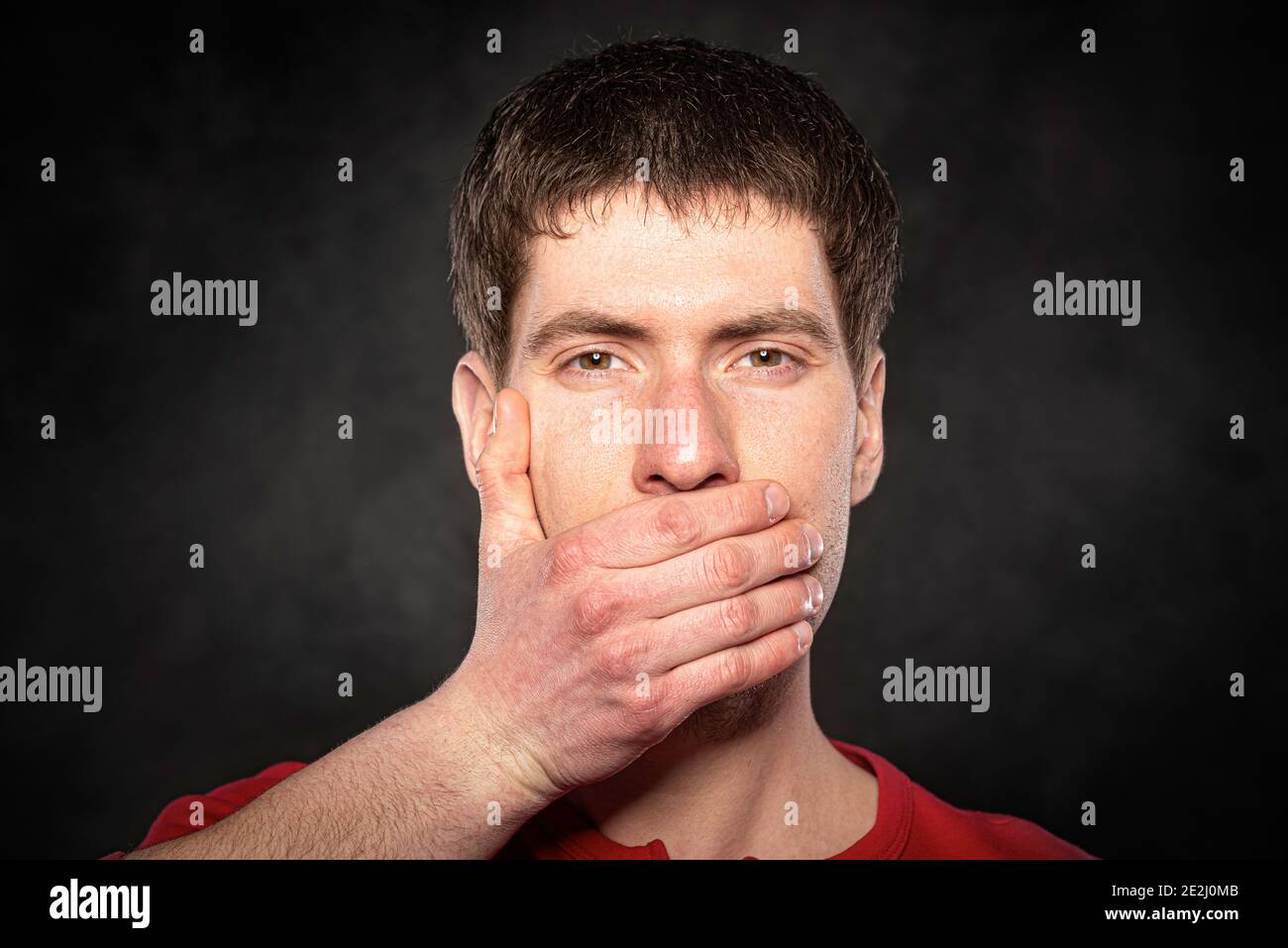 A man covers his mouth with his hand on a dark background Stock Photo ...